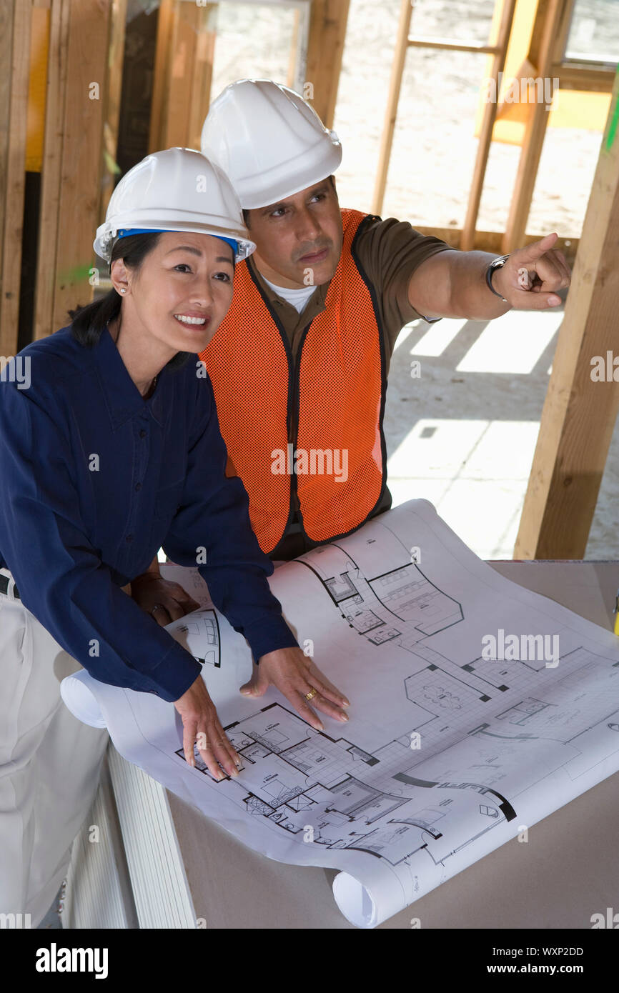 Architect and construction worker looking up at ceiling with blueprints ...