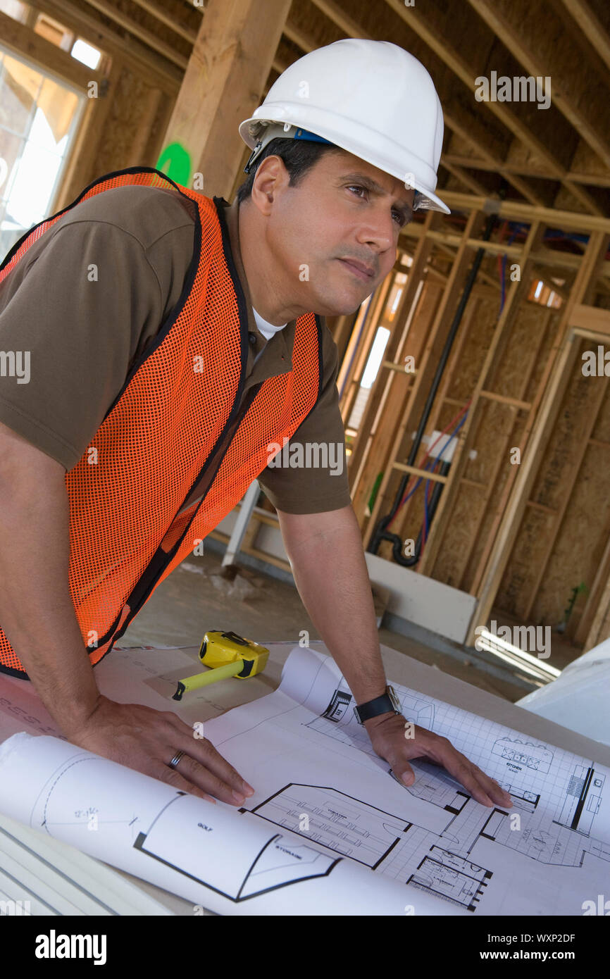 Construction worker examining blueprints inside half constructed house ...