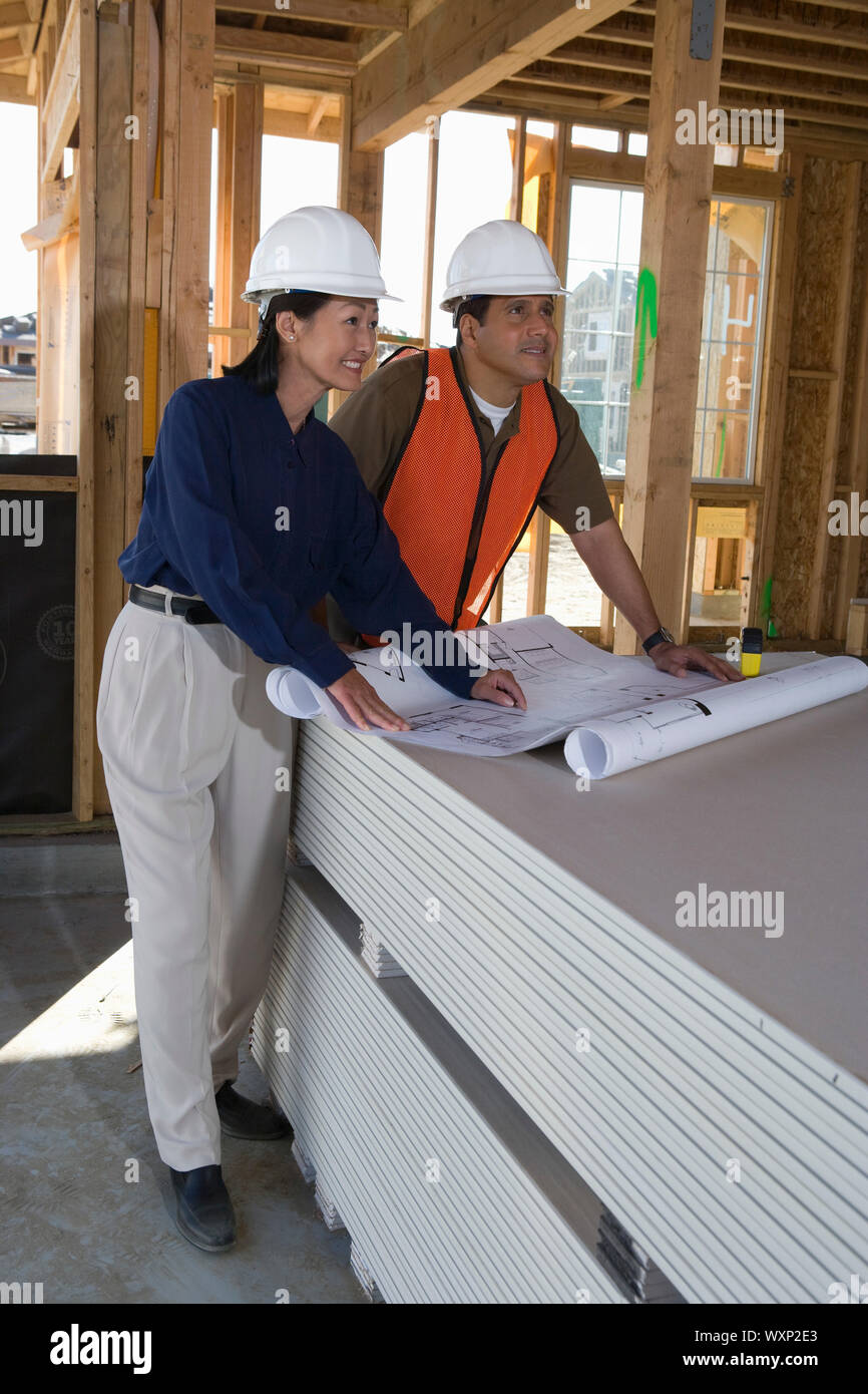 Architect and construction worker looking at blueprints inside half ...
