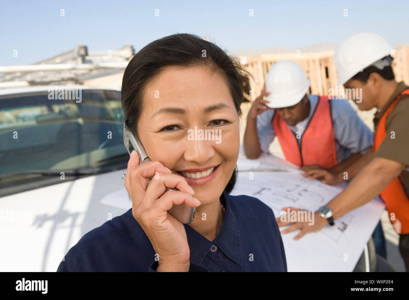 Two construction workers looking at blueprints and architect talking on ...