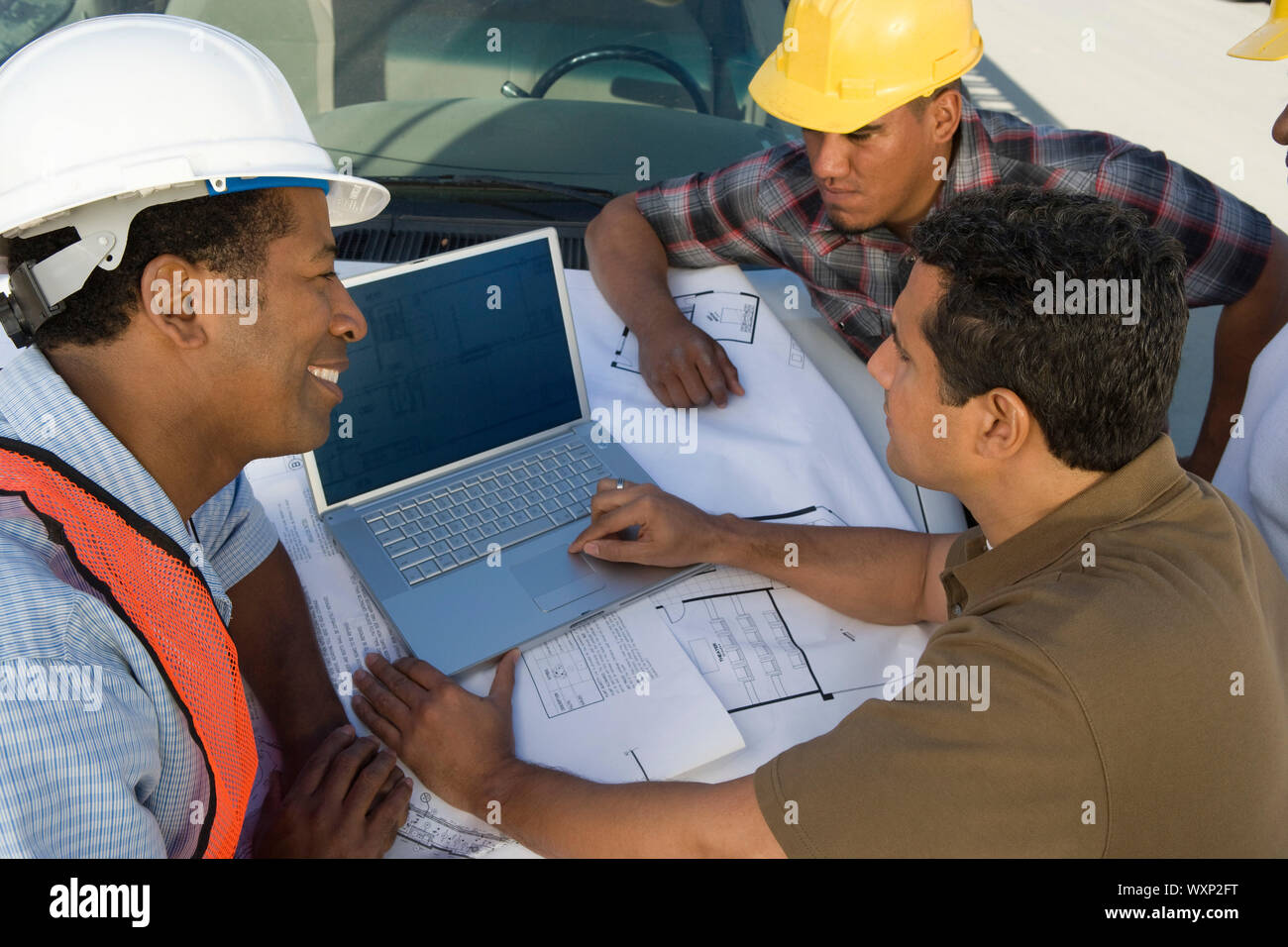 Four construction workers standing in front of car on construction site ...