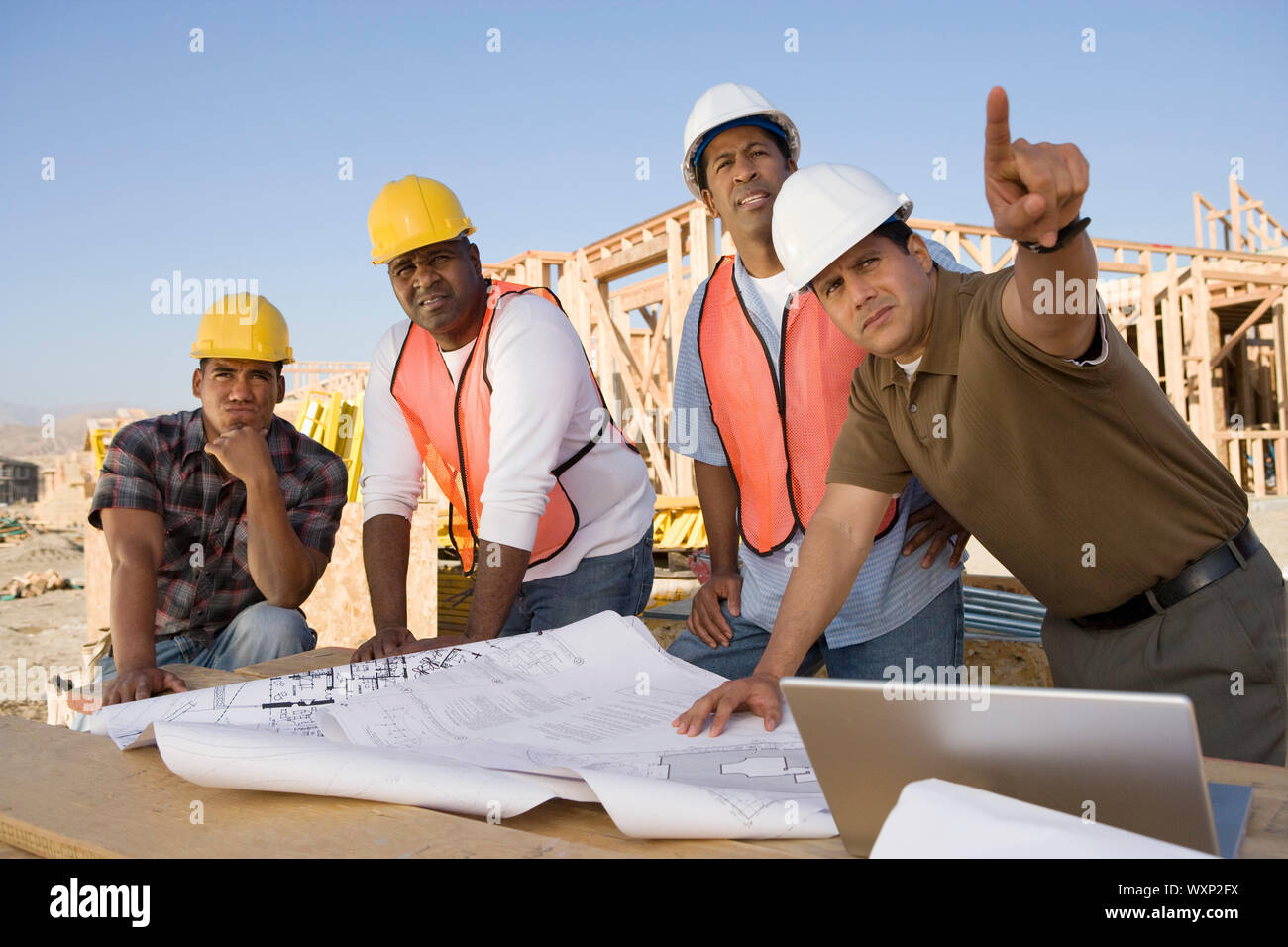 Four construction workers examining blueprints on construction site ...