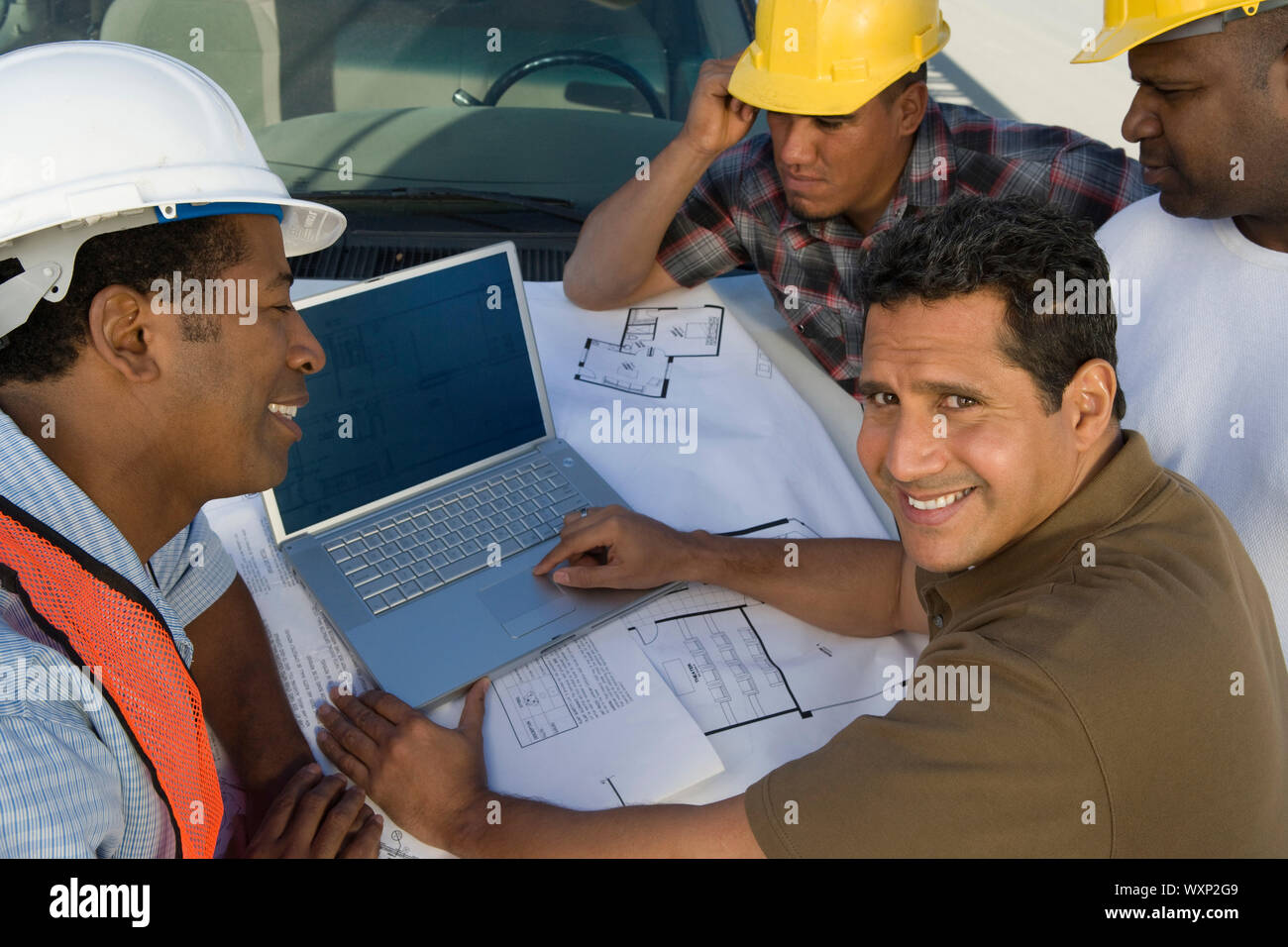 Four construction workers standing in front of car on construction site ...