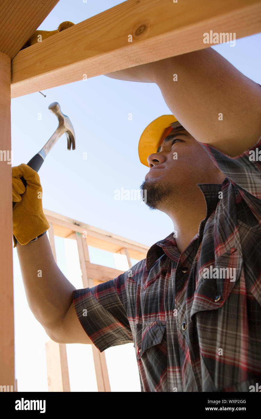 Construction worker hammering nail on construction site Stock Photo - Alamy