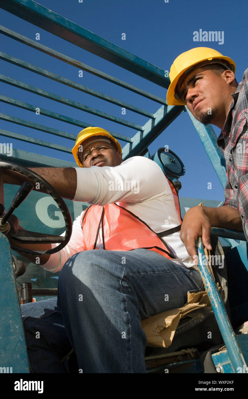 Construction worker sitting inside vehicle with another worker standing ...