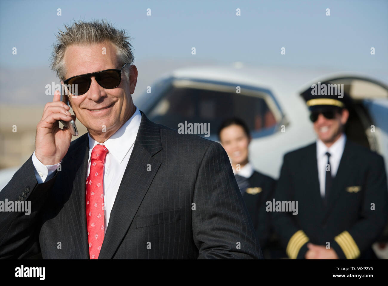 Mid-adult businessman talking on phone, pilot and flight attendant ...