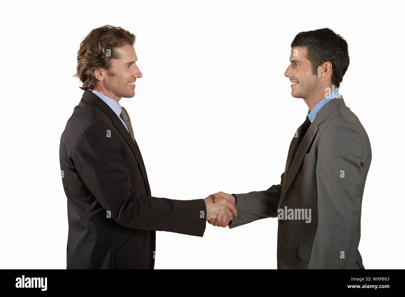 Side view of two young businessmen shaking hands on white background ...