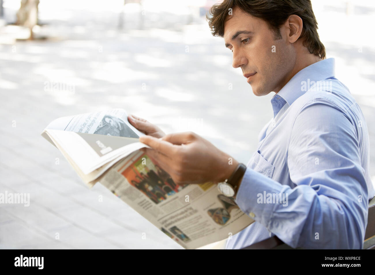 Side view of young businessman reading newspaper on bench outdoors ...