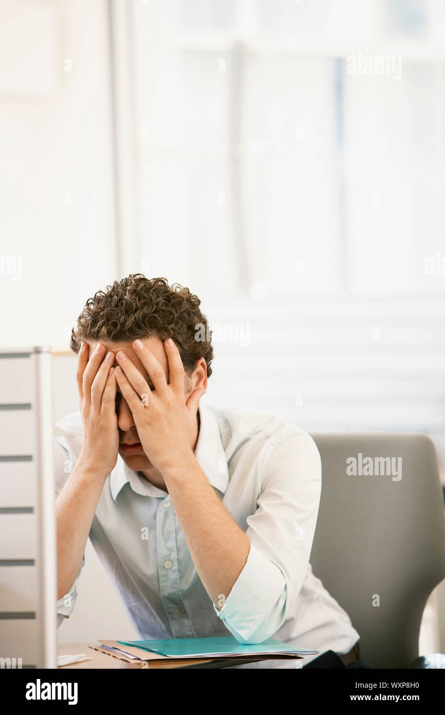 Stressed young male executive sitting in cubicle with head in hands ...