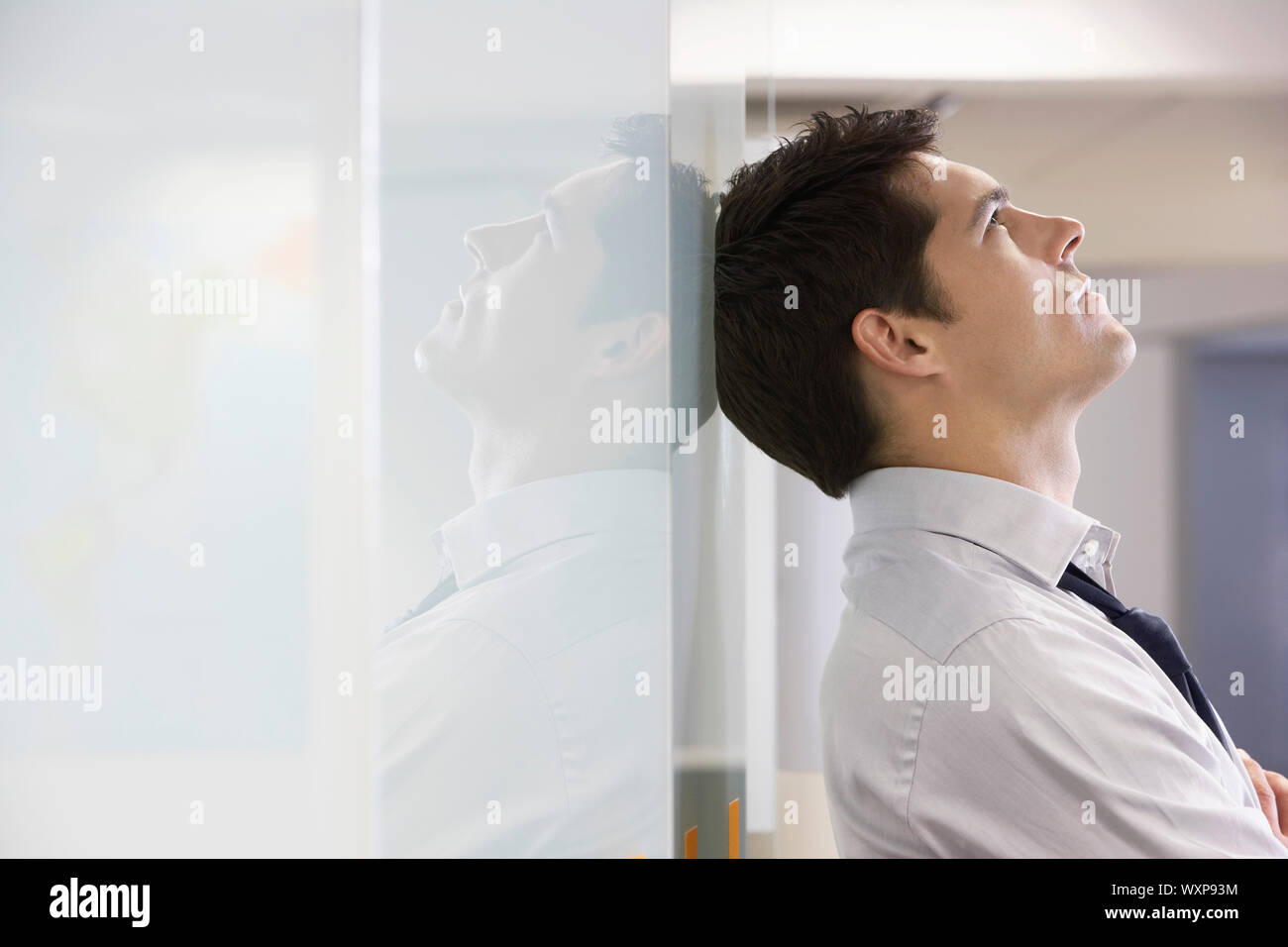 Unhappy businessman leaning back against office wall and looking at ...