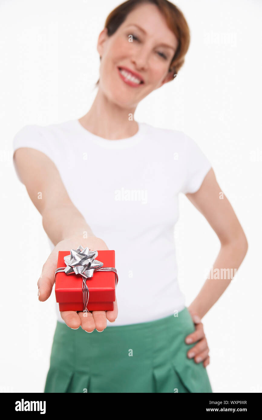 Portrait of young woman offering you a small wrapped gift against white ...