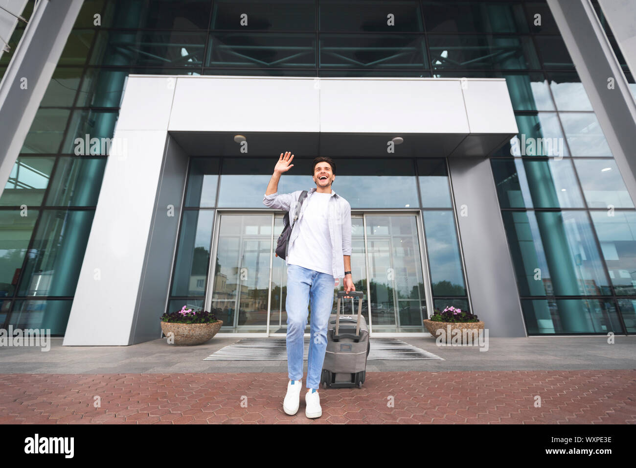 Happy man arrived home, waving hand while going out of airport building ...