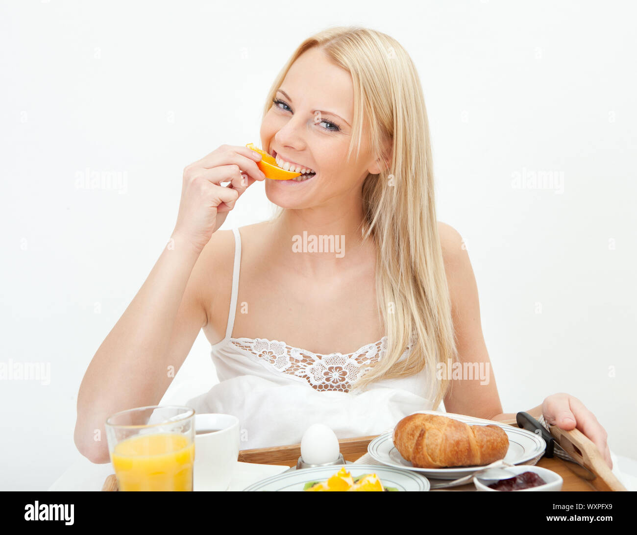 Beautiful woman eating orange in bed while eating breakfast Stock Photo ...
