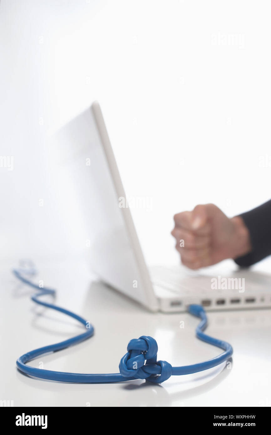 Closeup side view of hand hitting laptop keyboard with knotted cable ...