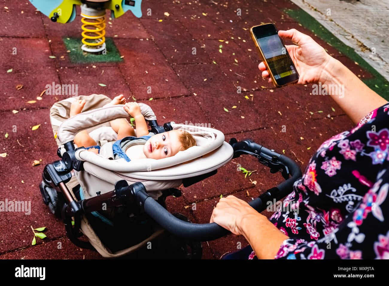Mother walks her baby while distracted uses her smartphone working on ...