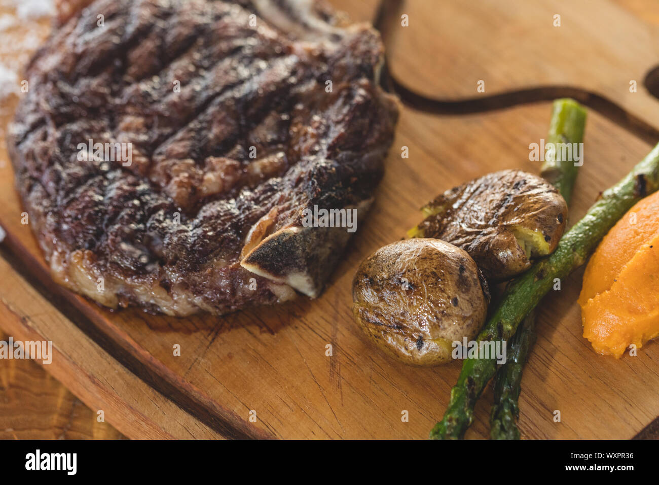 Grilled beef chop served on wooden serving plate with grilled ...