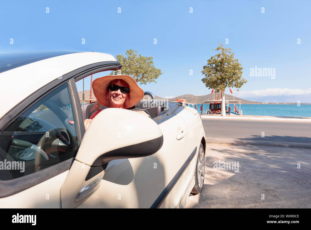 Single happy mature woman with hat and sunglasses driving her ...