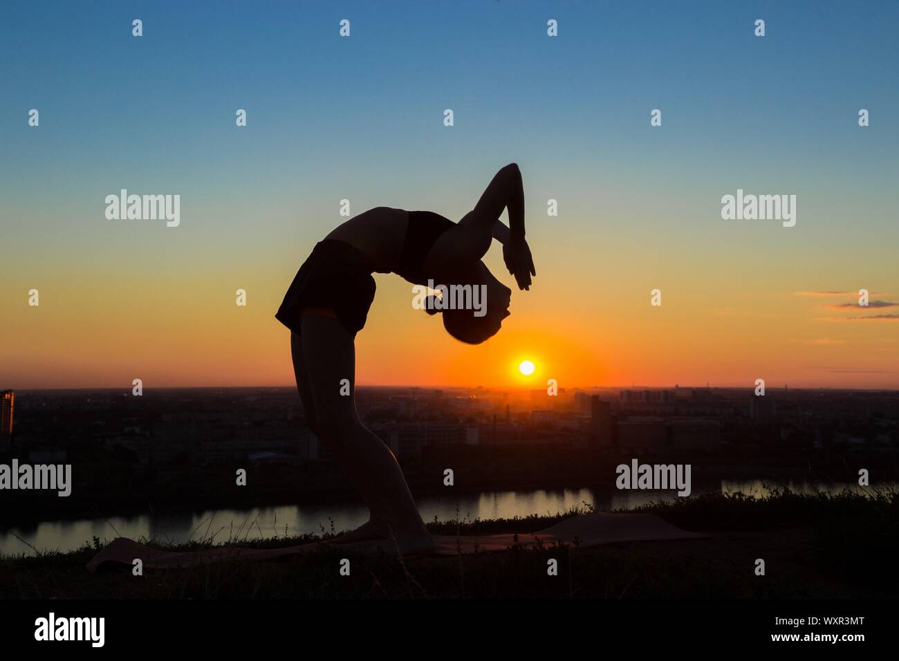 Silhouette of sporty woman practicing yoga in the park at sunset - drop ...