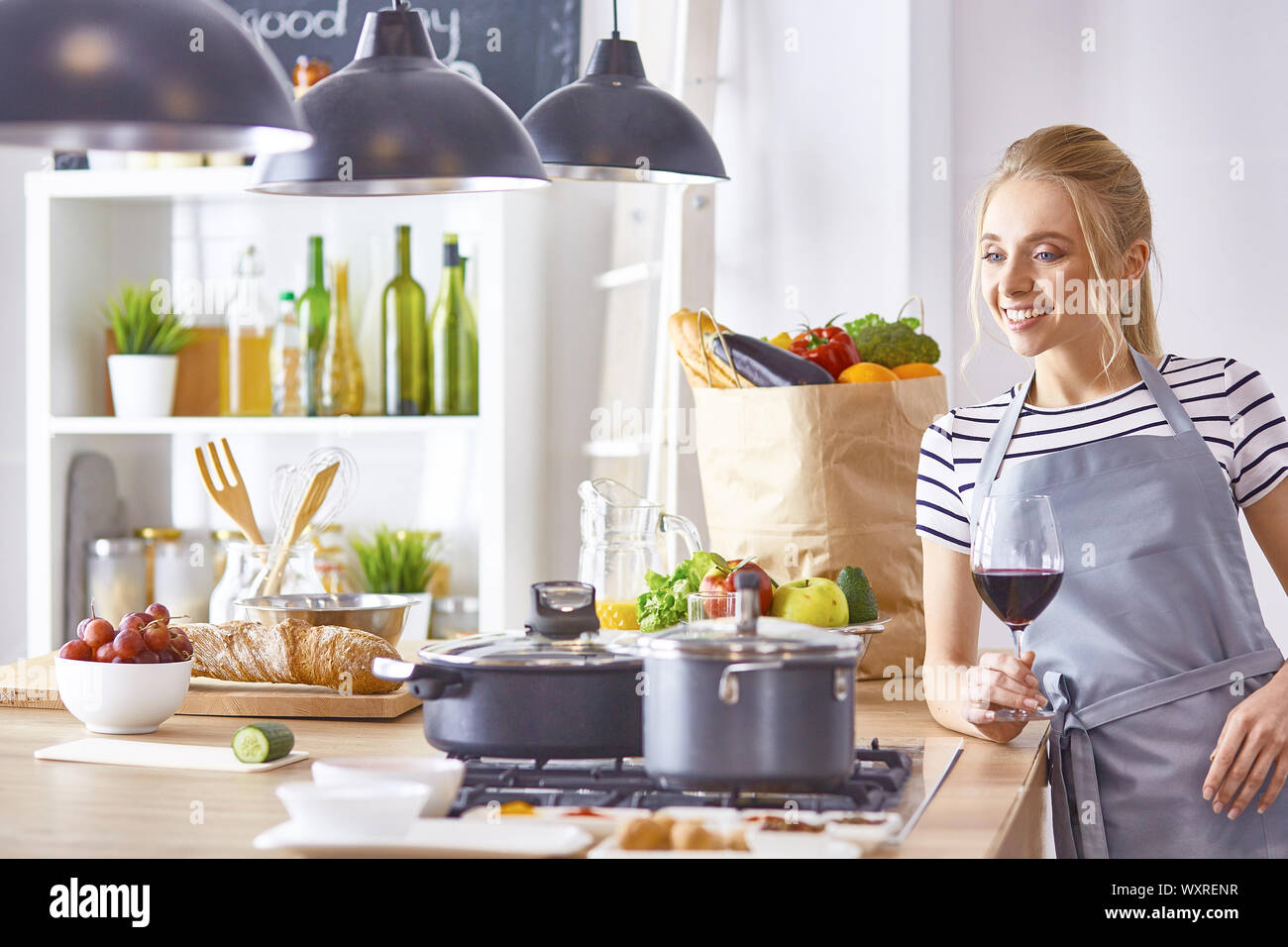 Beautiful woman in kitchen is drinking red wine Stock Photo - Alamy
