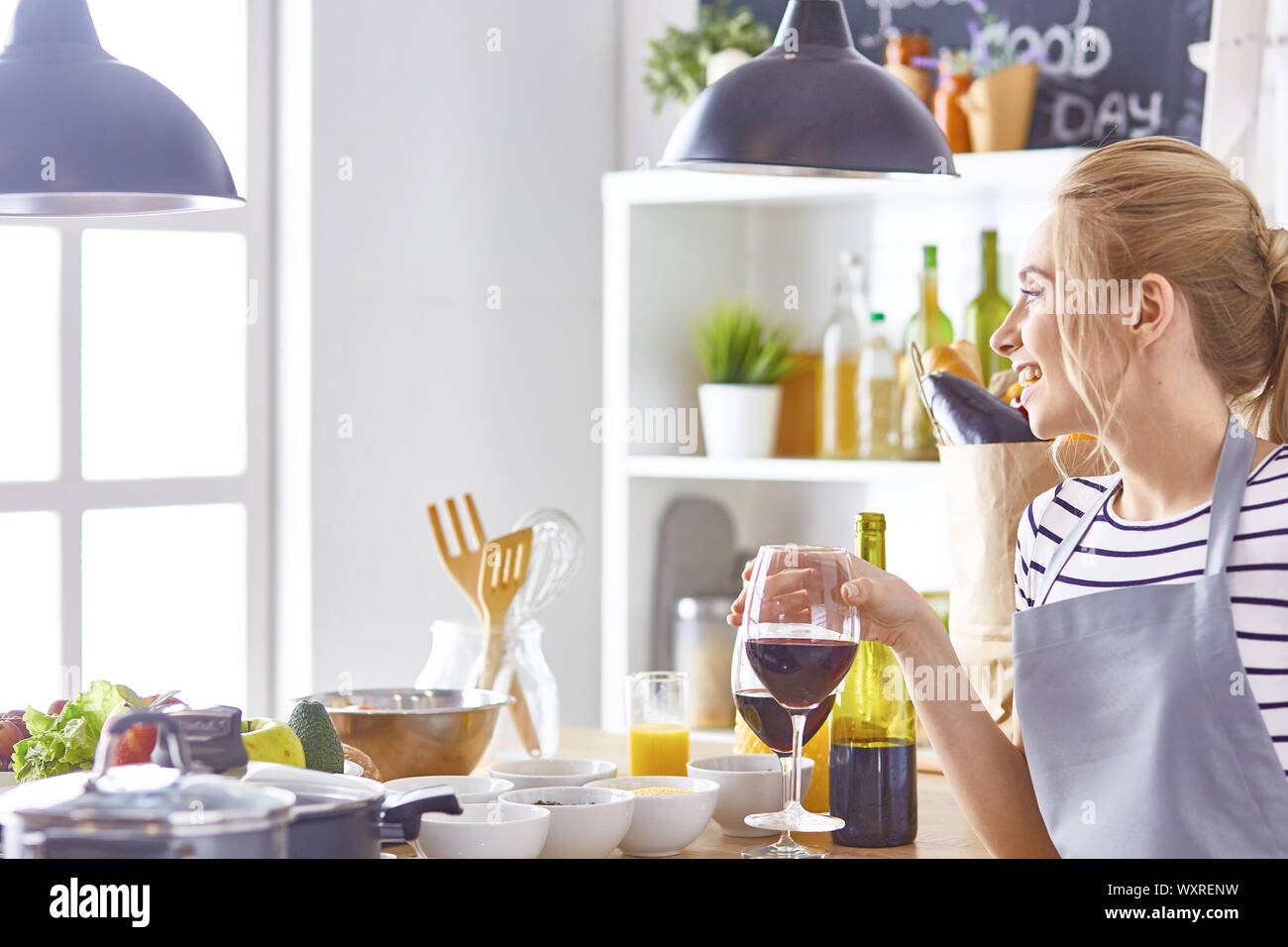 Beautiful woman in kitchen is drinking red wine Stock Photo - Alamy