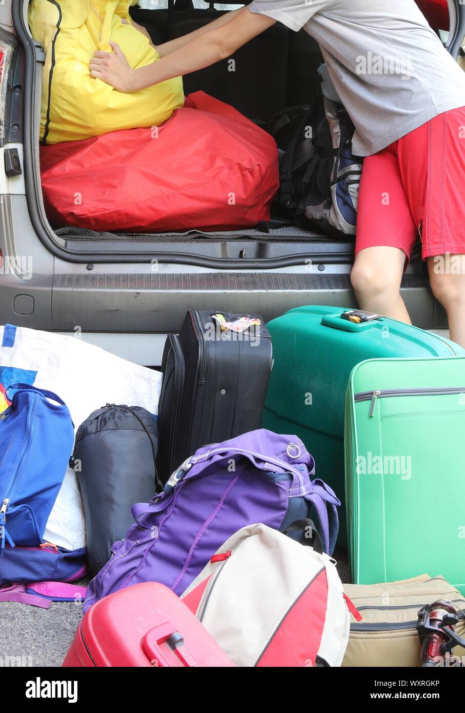 young boy loads the trunk of the car with a lot of luggage before the ...