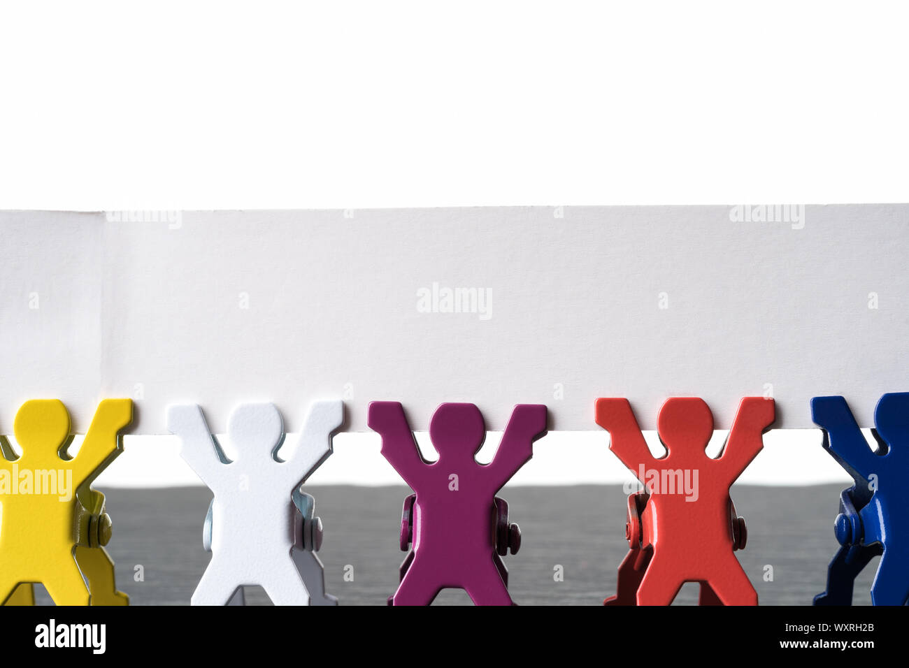 Colorful diverse miniature people figurines standing in a row on a dark ...