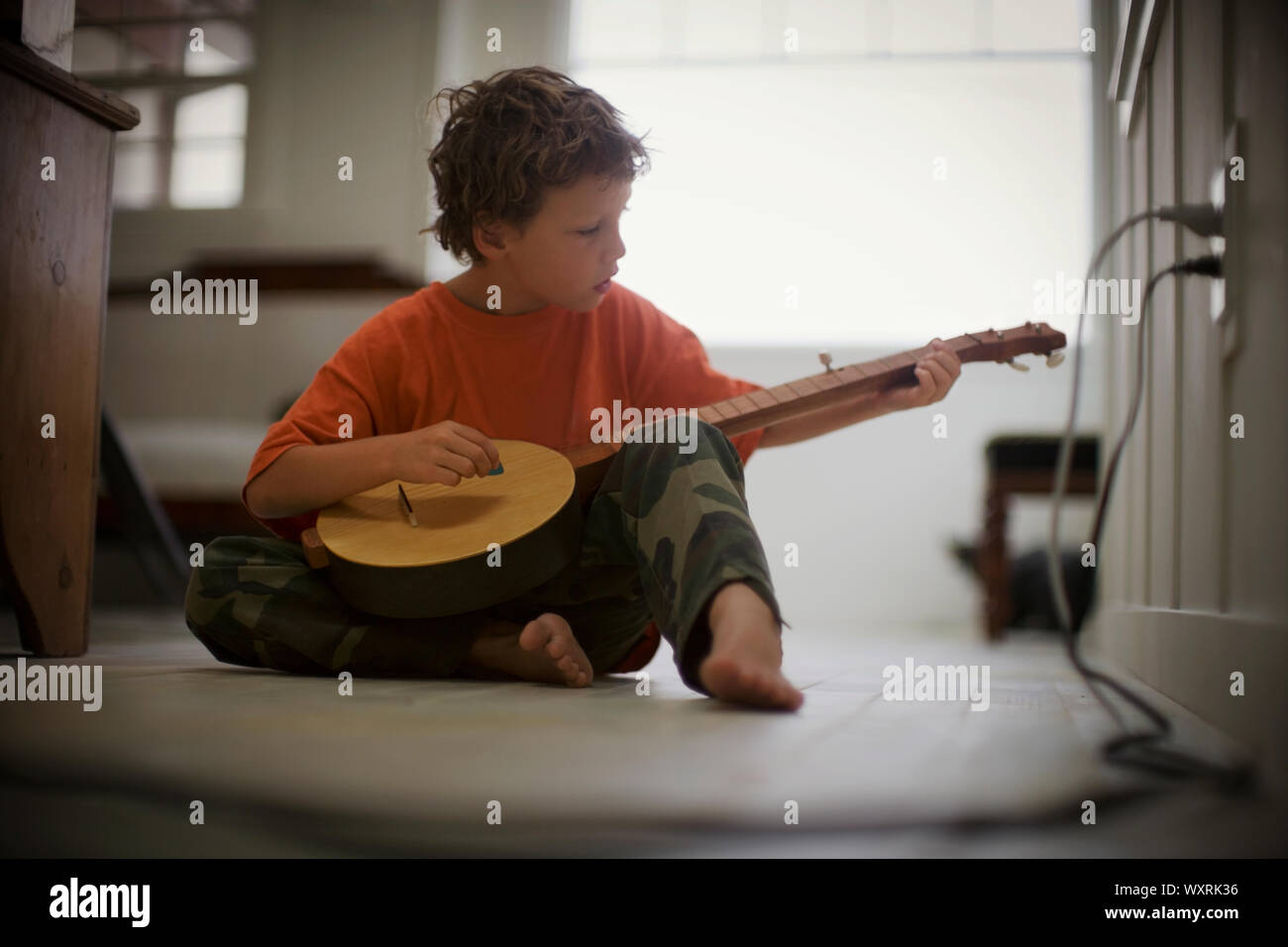 Young boy sitting on the floor playing a banjo Stock Photo - Alamy