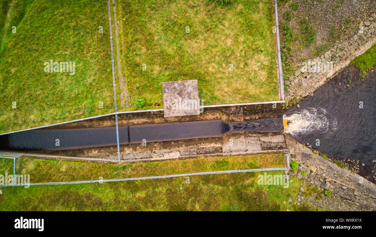 Aerial view of a spillway, Loch Turret Reservoir Dam. Blue water flows ...