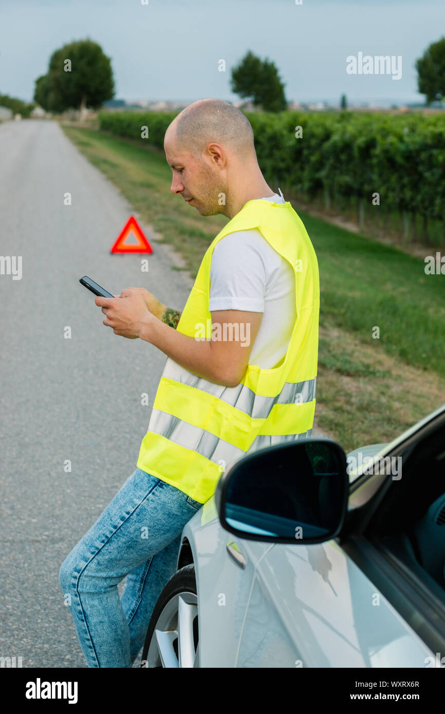 Young man calling roadside assistance after breaking down with his car ...