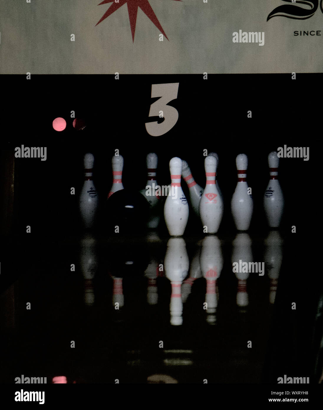 Bowling lane with bowling ball striking bowling pins with red stripes ...