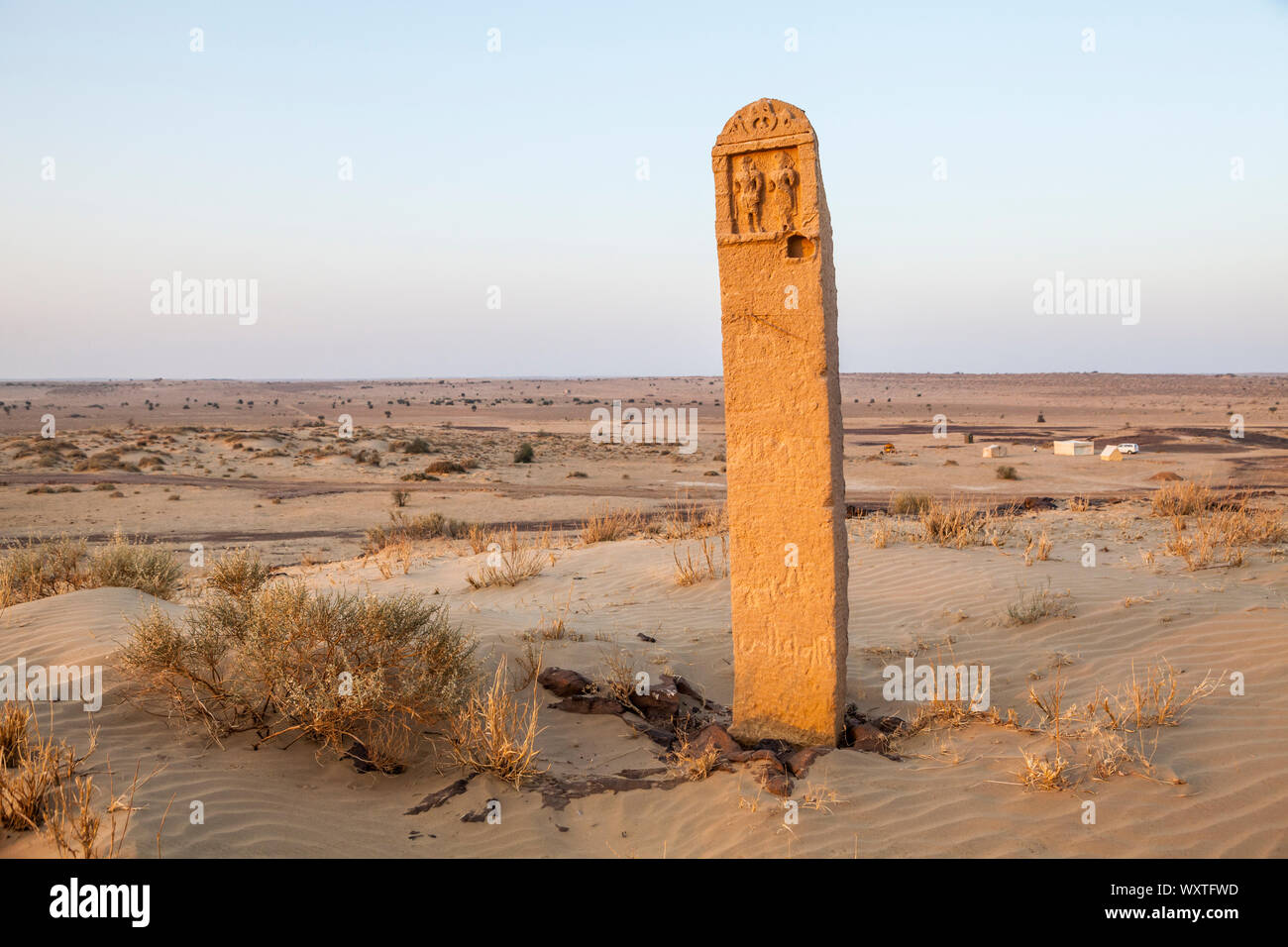 A stone marker on a sandy hill above a camp which is part of a tourist ...