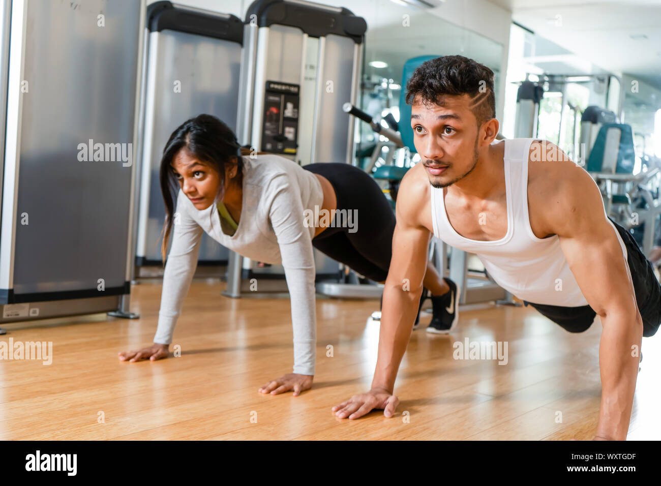 Cheerful young couple exercising forearm plank side by side on mats ...