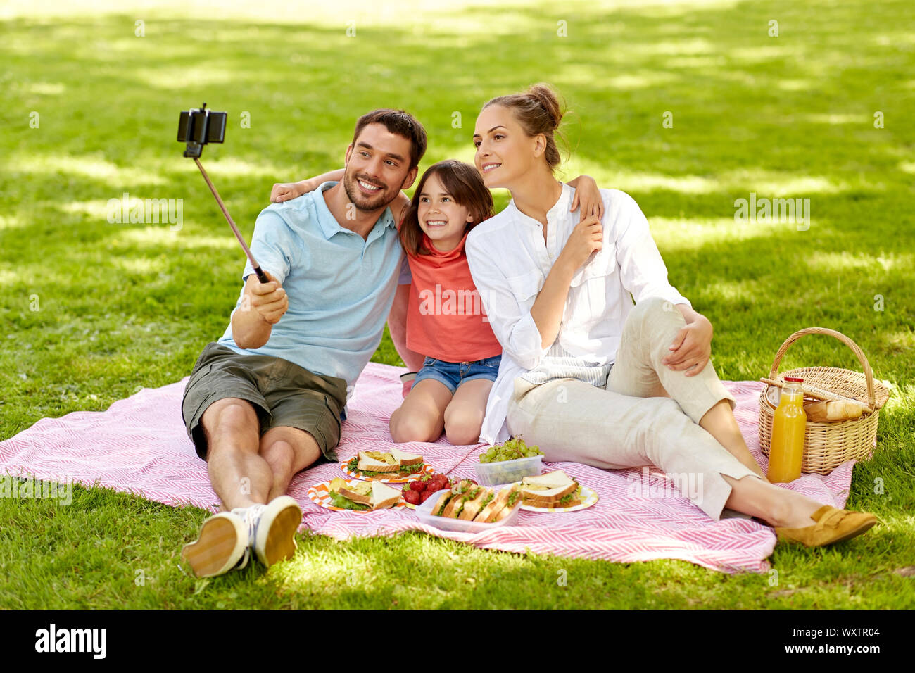 family, leisure and technology concept - happy mother, father and daughter having picnic and ...