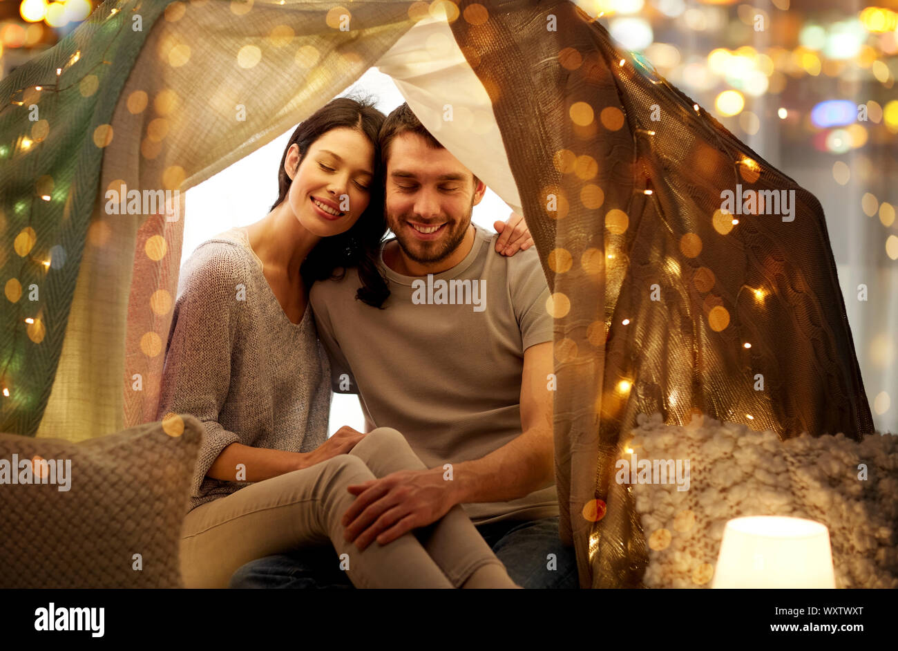 leisure, hygge and people concept - happy couple in kids tent at home ...
