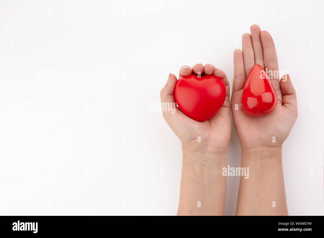 Two hands holding red blood drop and heart on white background. Give ...