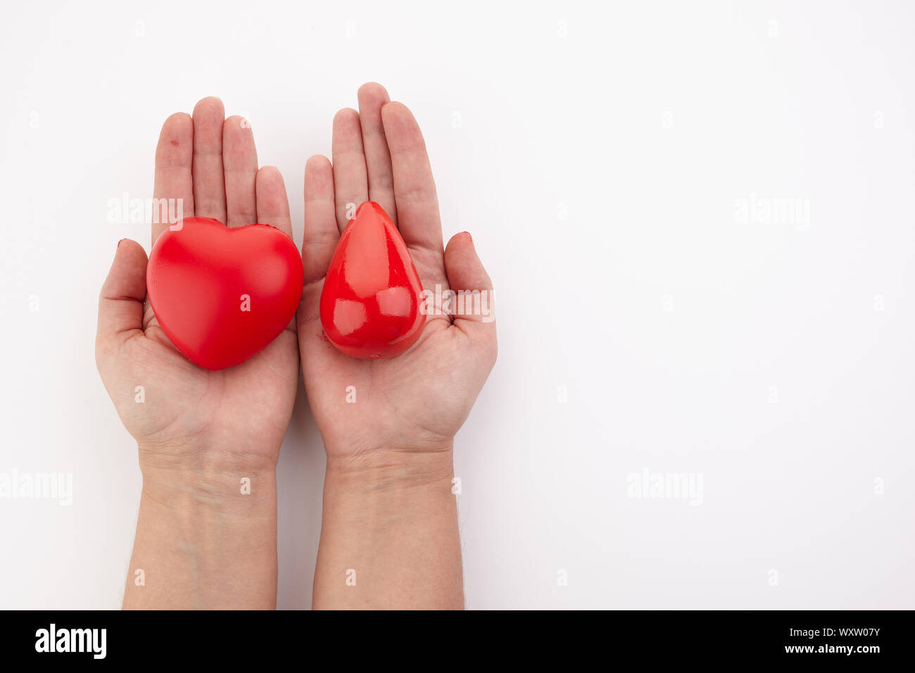 Two hands holding red blood drop and heart on white background. Give ...