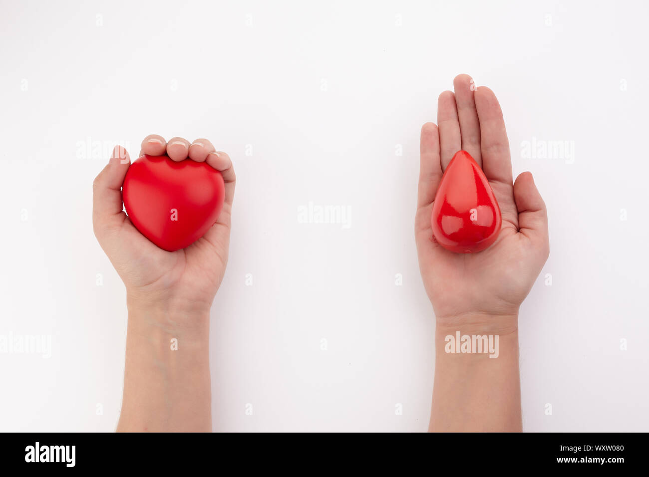 Two hands holding red blood drop and heart on white background. Give ...