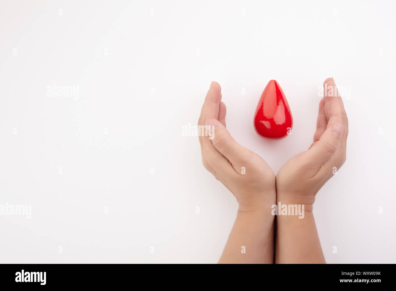 Two hands holding red blood drop on white background. Give blood ...