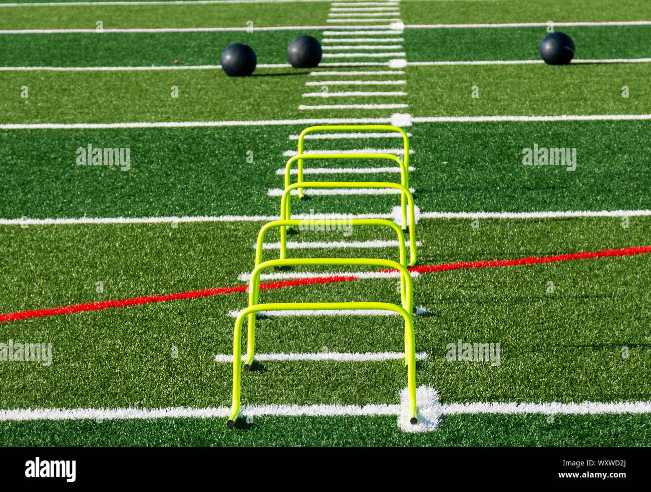 A turf field is set up with six yellow mini hurdles and three medicine balls for strength ...