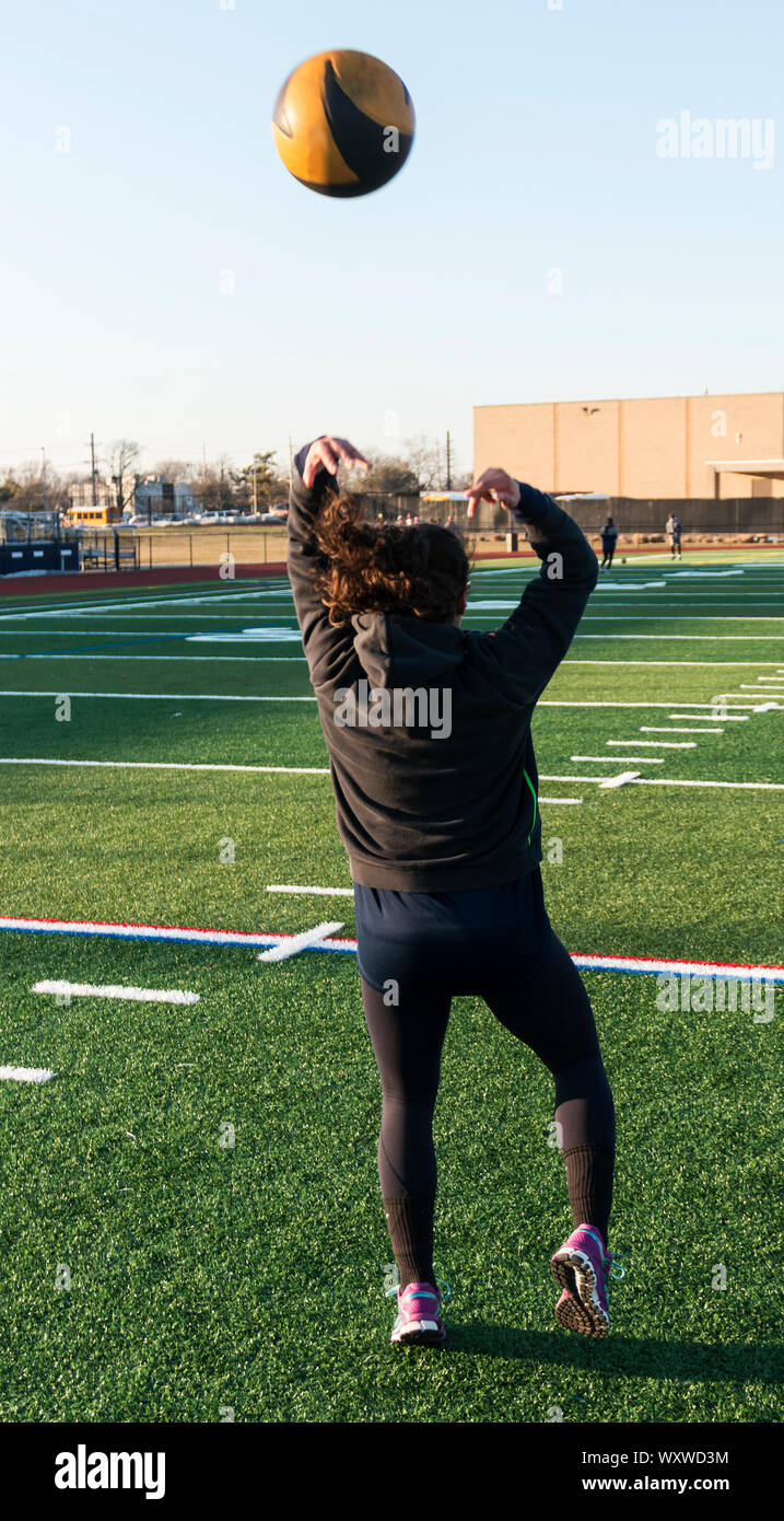 An athlete is on a green turf field throwing a black and gold medicine ...