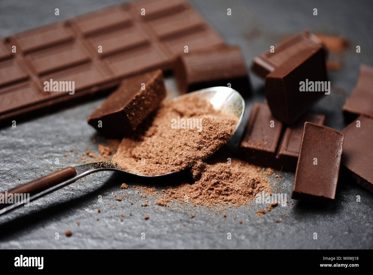 chocolate bar and chocolate powder on spoon on the dark background ...
