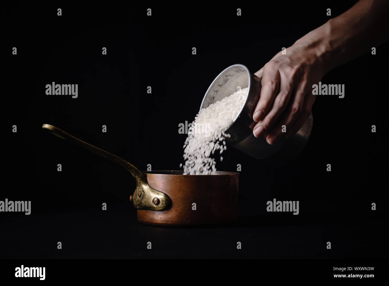 Female hand pouring arborio rice to copper saucepan for boiling. Dark ...
