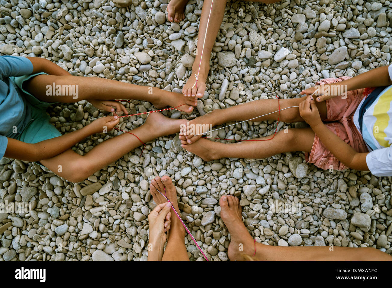 Top view of four children sitting on pebbles making knotted bracelets ...