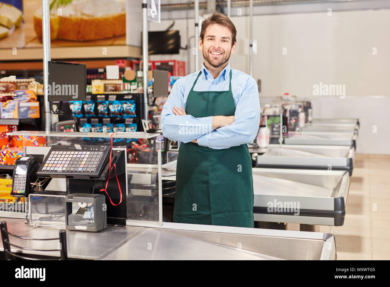 Smiling cashier or salesman in green apron at the supermarket cashier ...