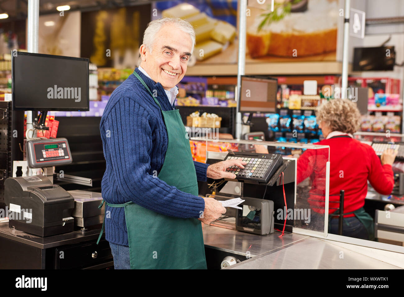 Friendly cashier with green apron at the cash register in the ...