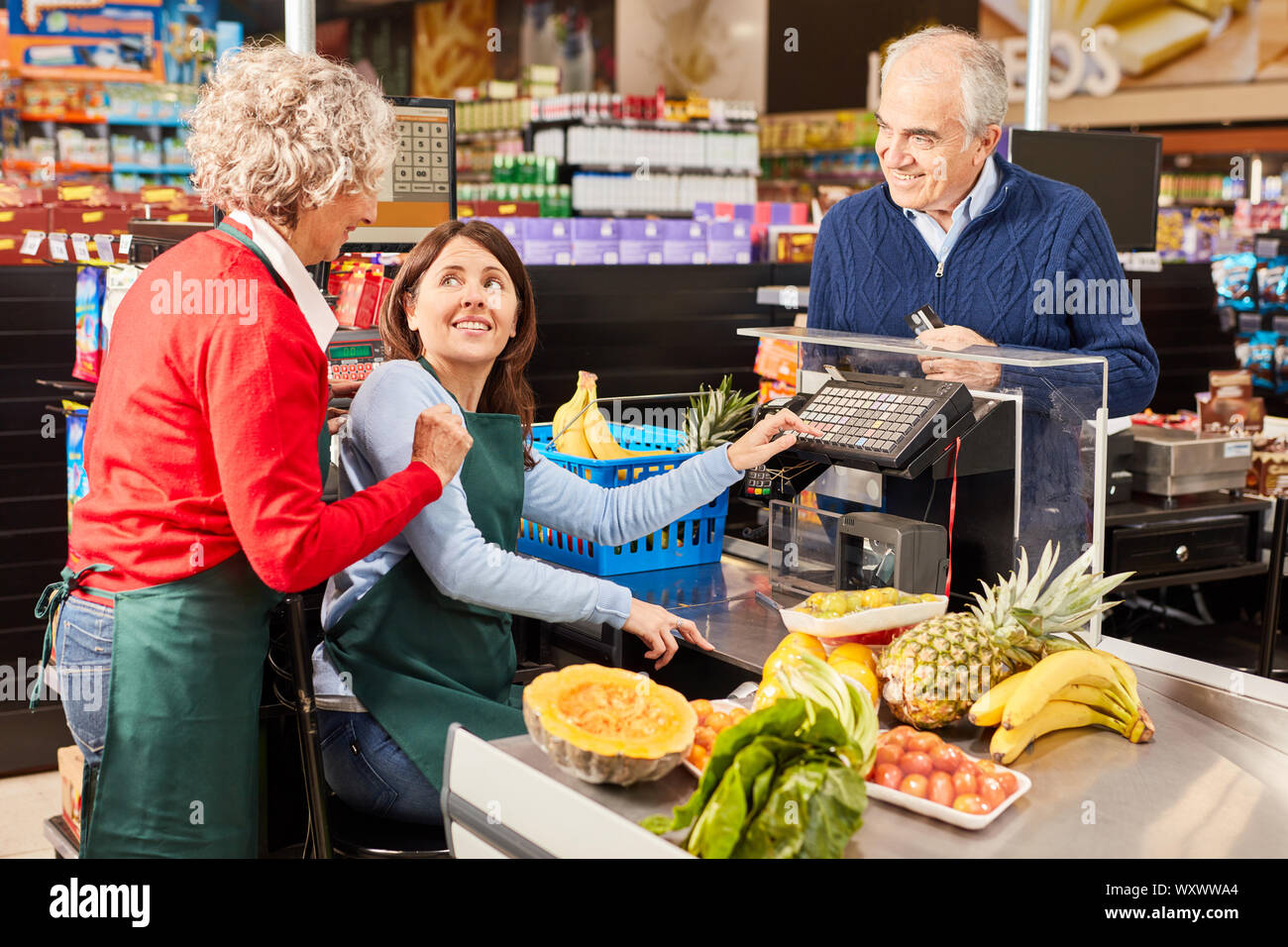 Employee helps young woman as a cashier trainee at the cashier in the ...