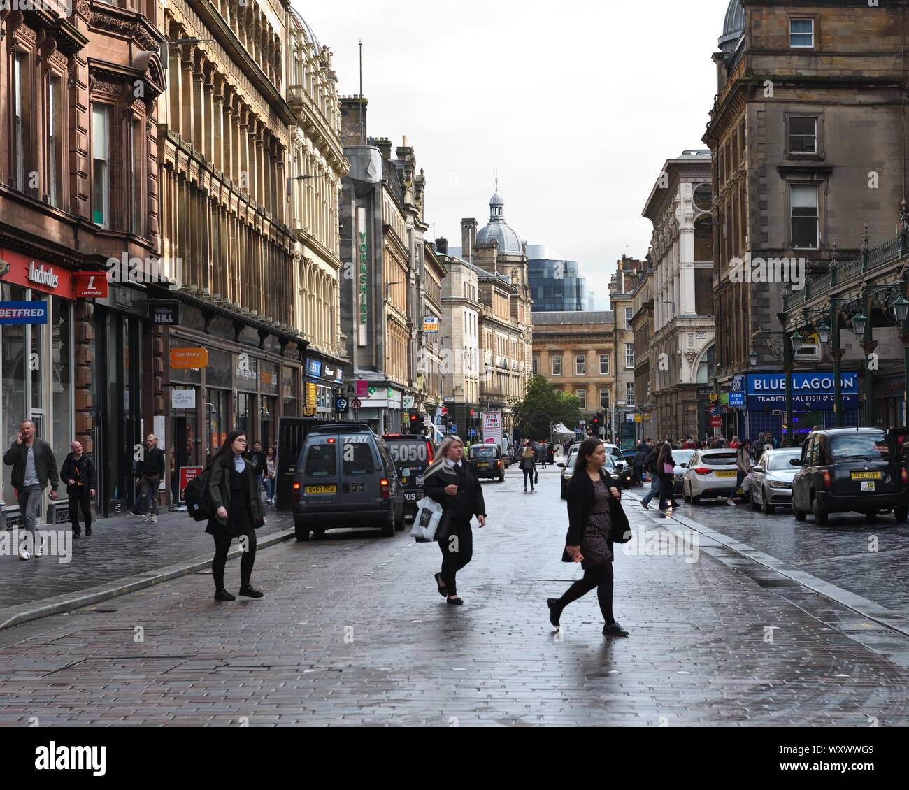 City view of people crossing the wet cobbled road looking east on ...