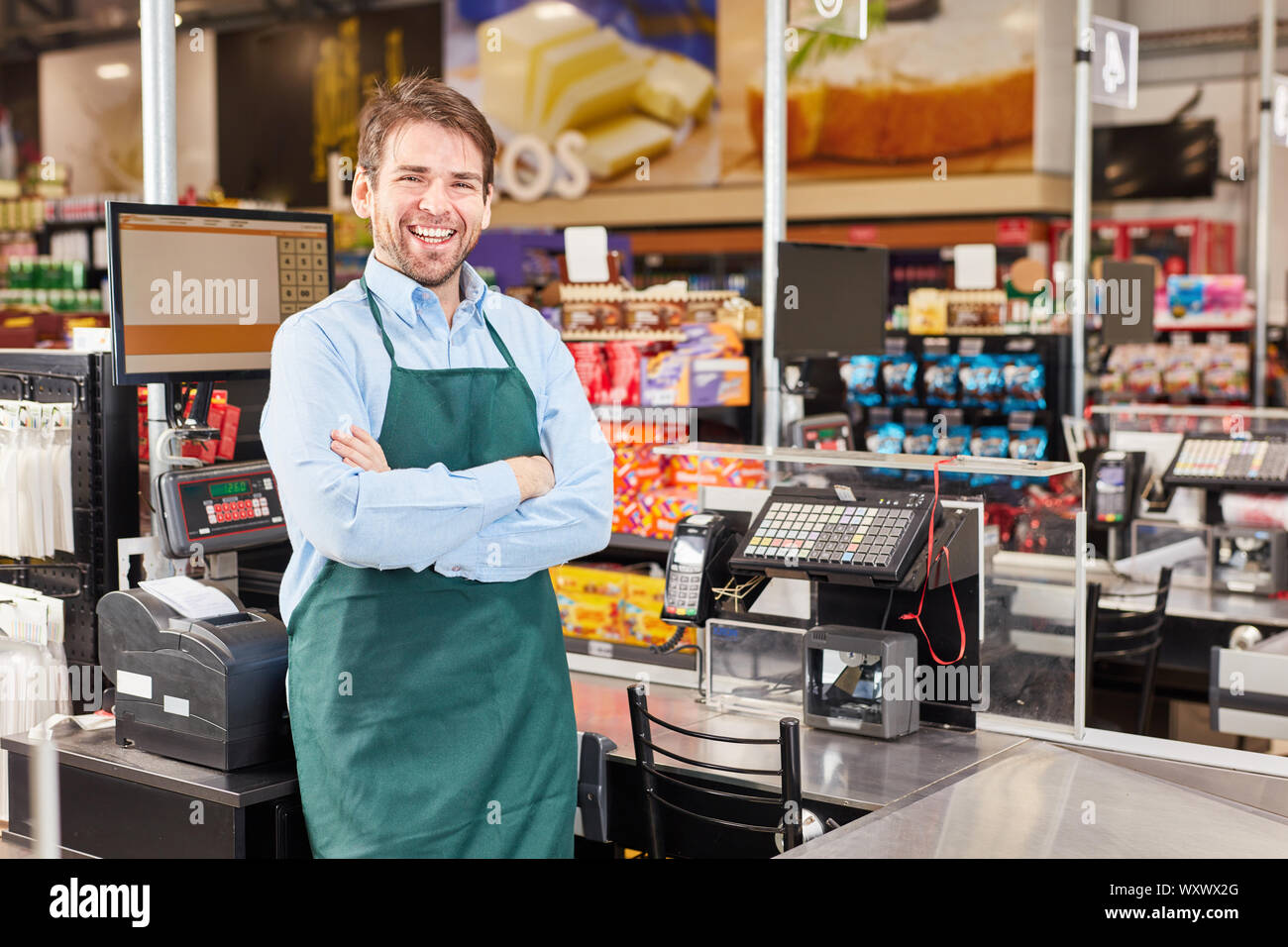 Cheerful man as a cashier with crossed arms in the supermarket at the ...