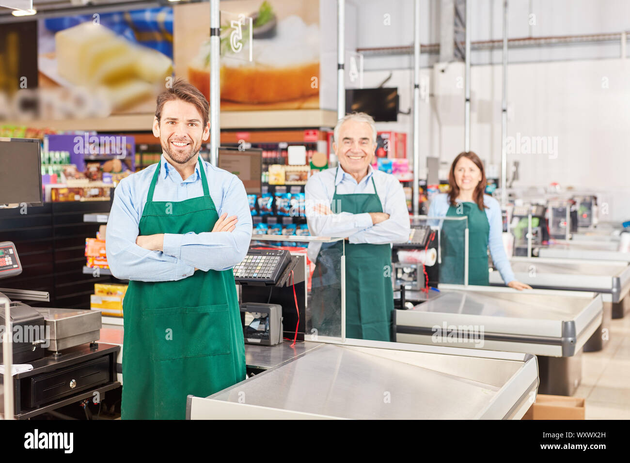 Three supermarket staff at checkout as a friendly colleague team Stock ...