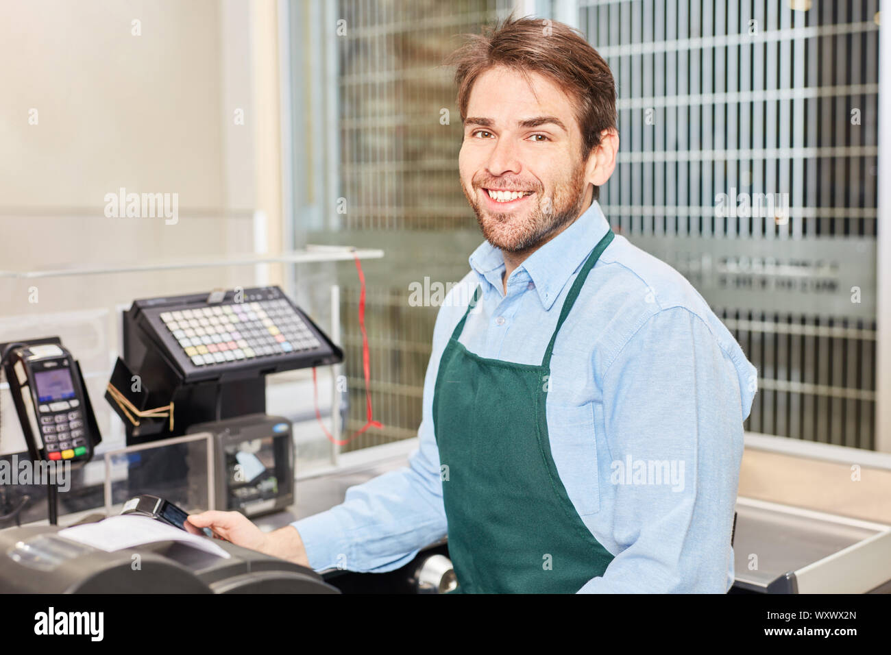 Smiling young man as a friendly cashier at the cash register in the ...